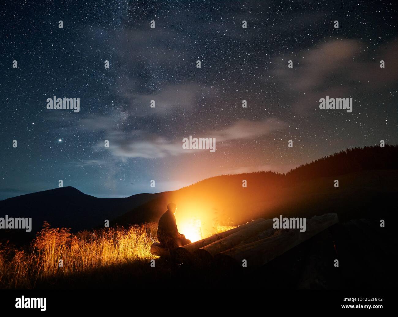 Tourist man resting on nature and enjoying bonfire under starry sky ...