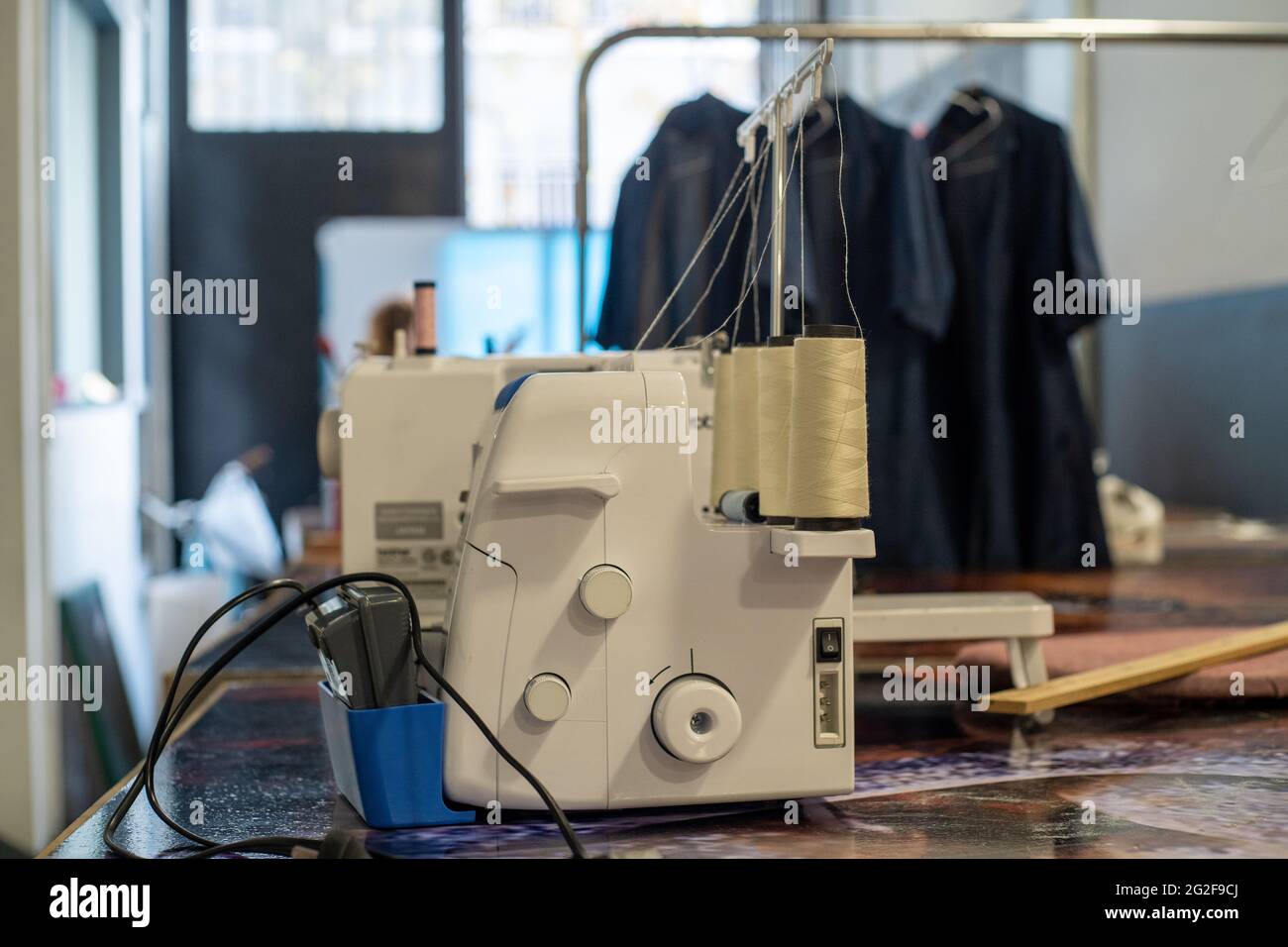 Closeup of overlock sewing machine on the table with hanged black coats ...