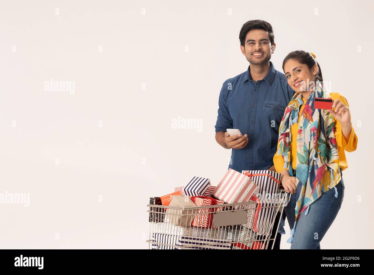 A MODERN COUPLE STANDING WITH GIFTS TROLLEY WHILE HOLDING DEBIT CARD ...