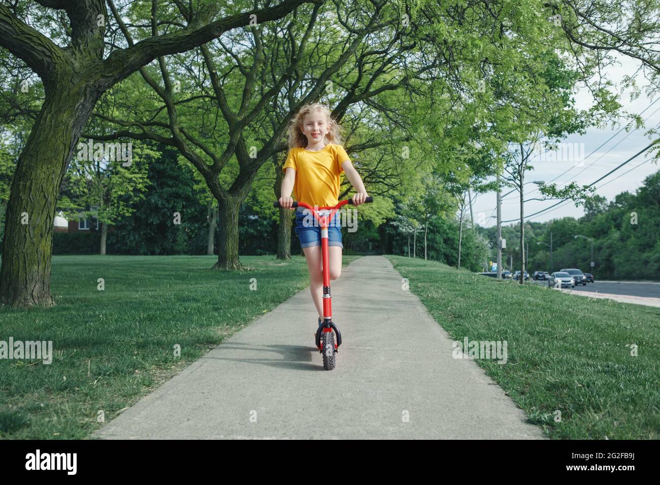 Cute funny Caucasian girl child in yellow t-shirt riding red scooter on ...