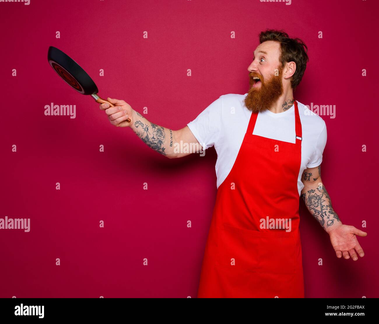 Happy chef with beard and red apron cooks with pan Stock Photo - Alamy