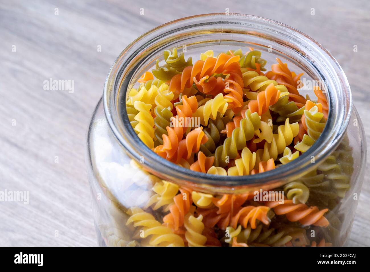 A glass pot, jar or bowl full of spirelli in three different colors ...