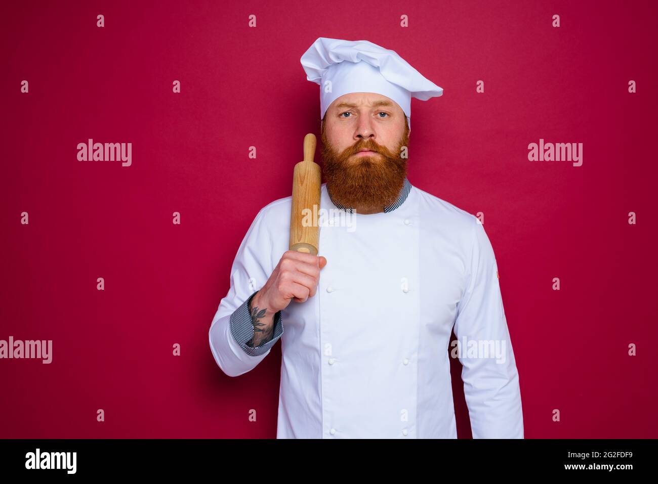 serious chef with beard and red apron chef holds wooden rolling pin ...