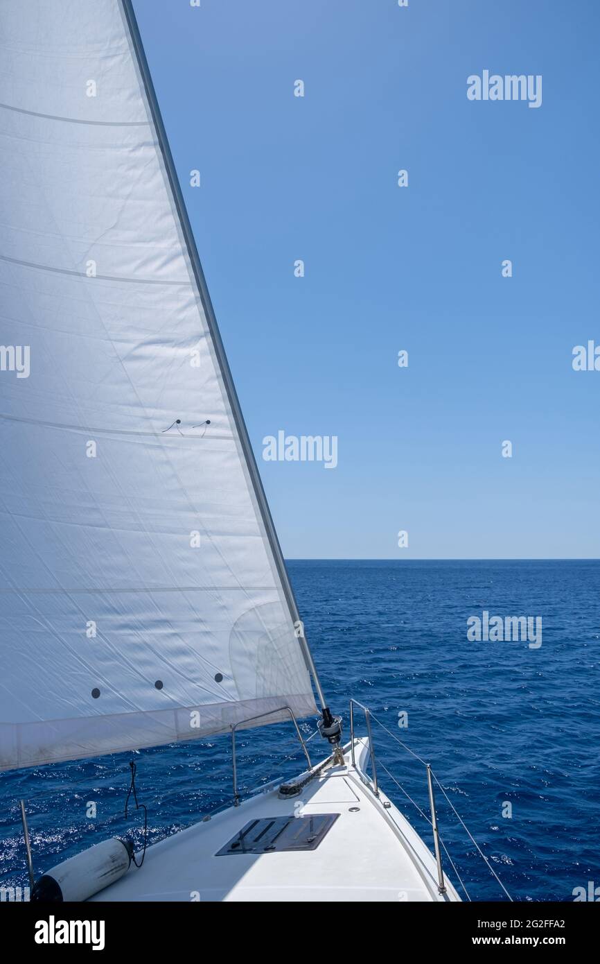 White sloop rigged yacht sailing in open calm ocean, blue sky ...