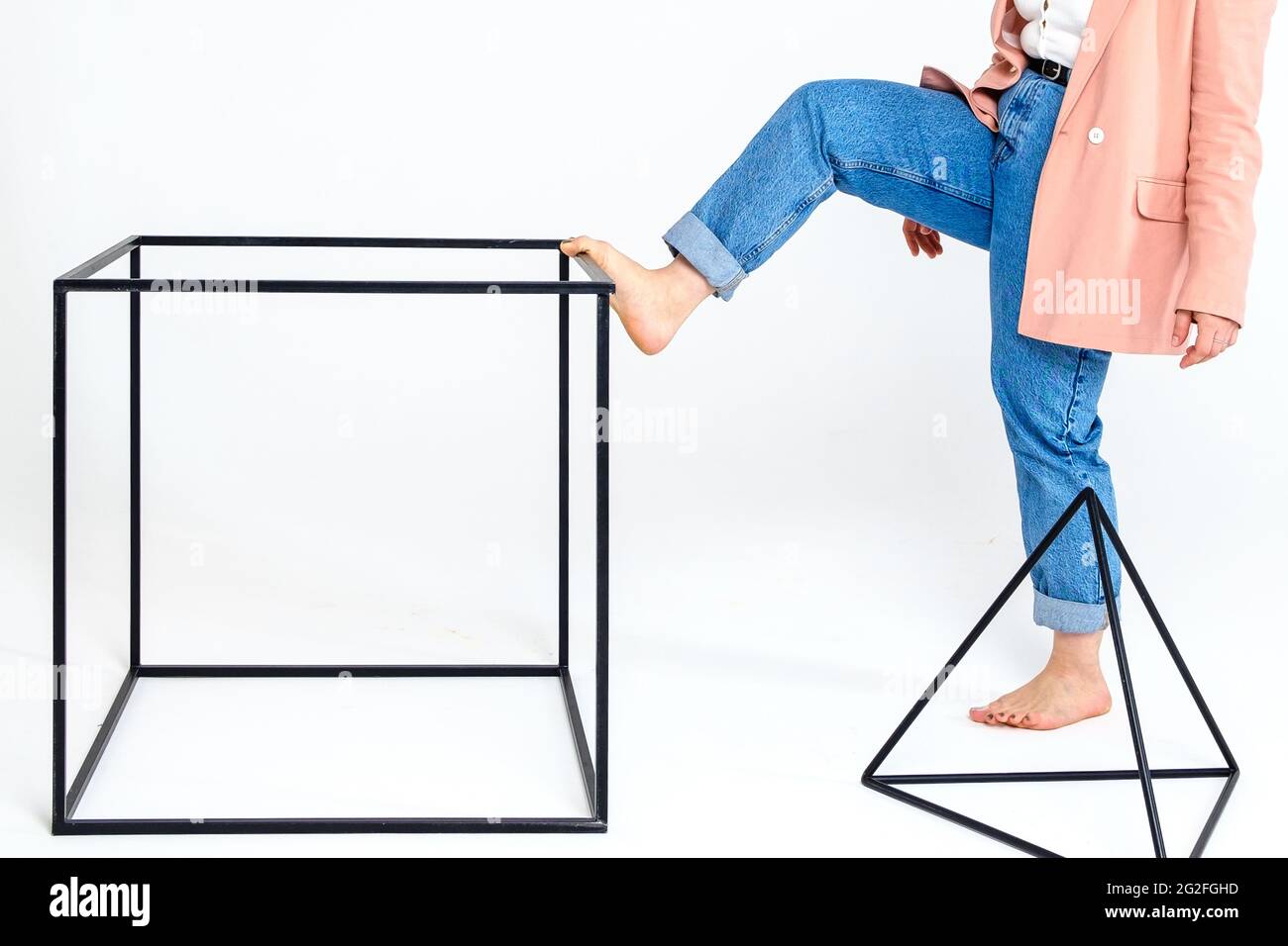 A young woman in jeans stands barefoot with her leg thrown over the ...