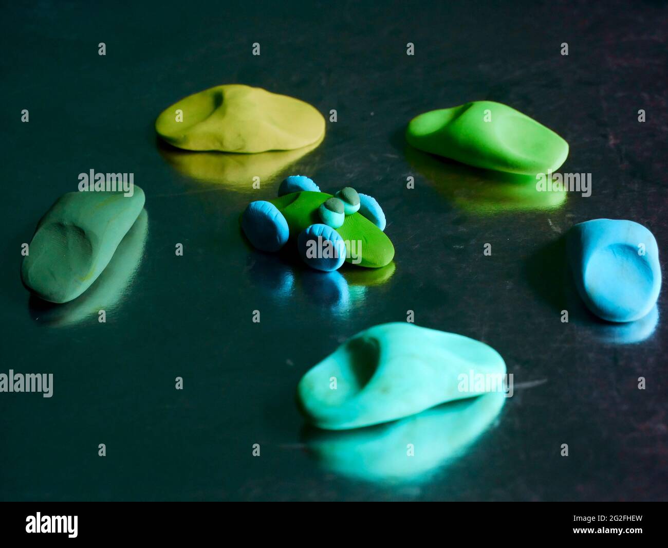 Green color clay car with semi finished cars circle on glass surface ...