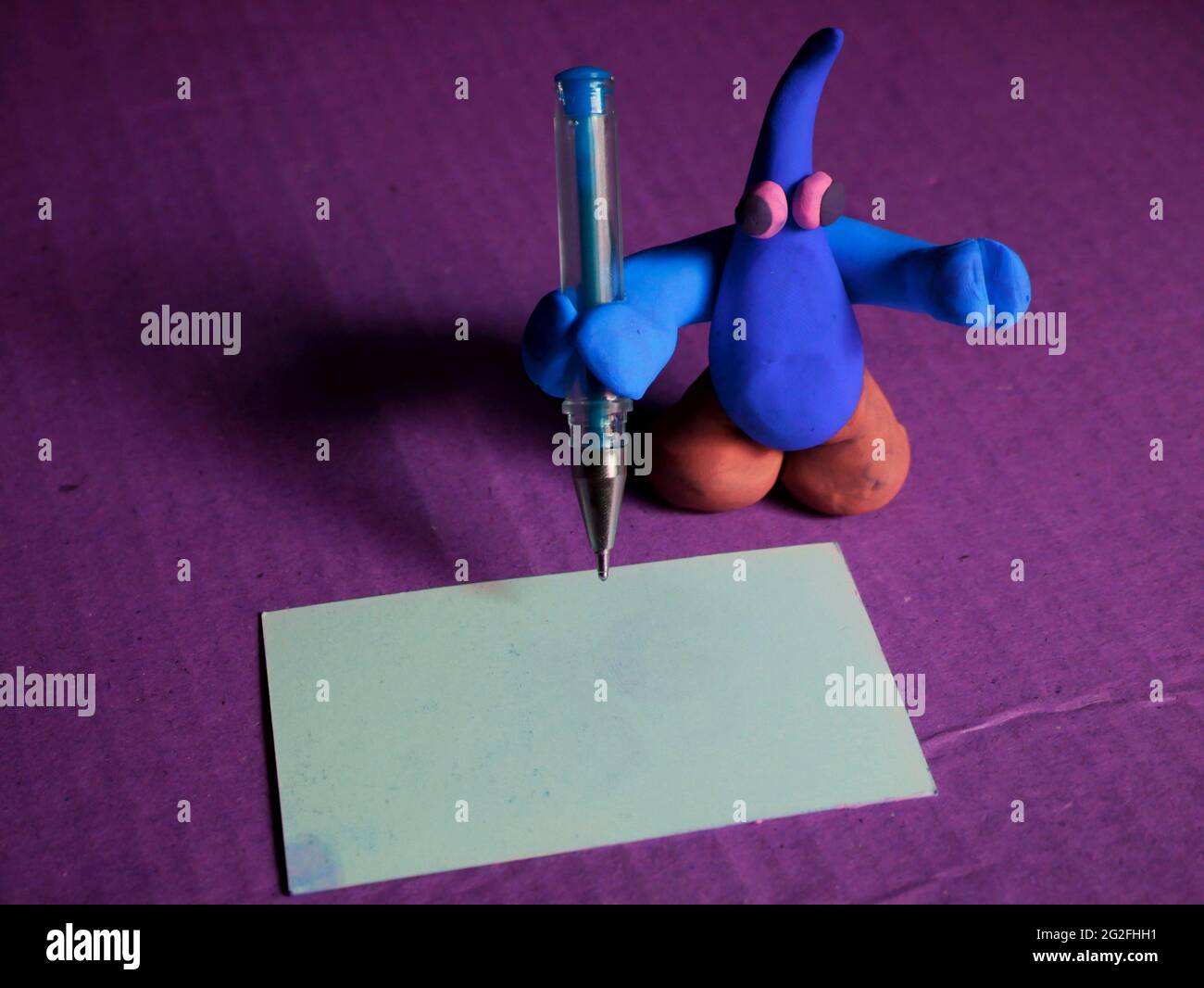 Blue cartoon clay toy holding pen on hand for writing on white card ...