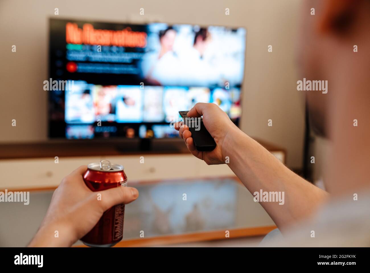 Caucasian guy drinking soda and using remote control while watching TV ...