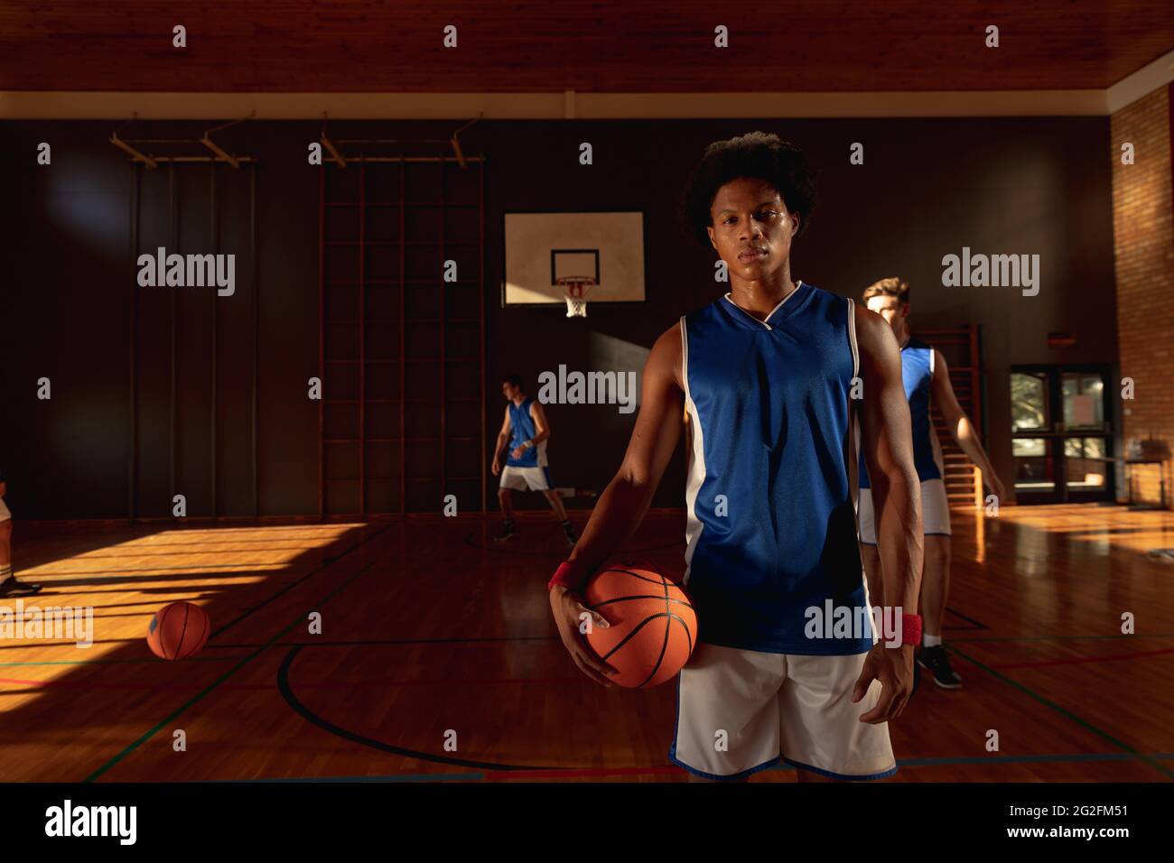 Portrait of mixed race male basketball player with team in background ...
