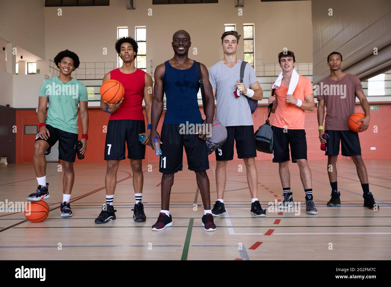 Portrait of diverse male basketball team and coach smiling and holding ...