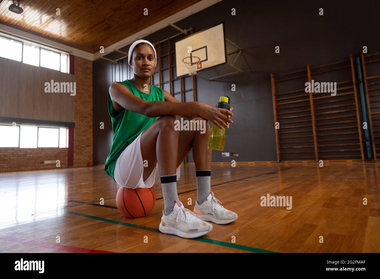 Portrait of mixed race female basketball player sitting on ball Stock ...