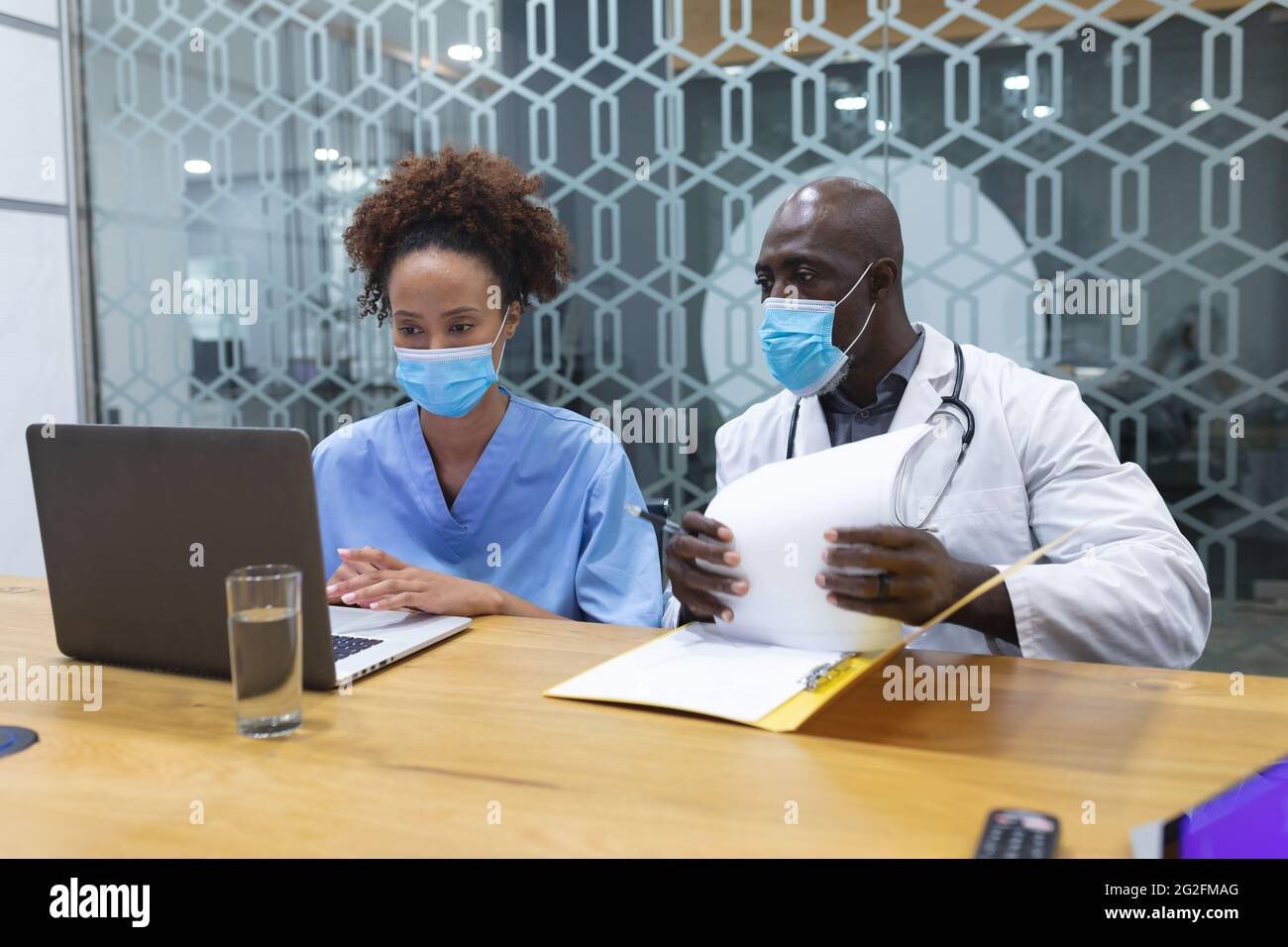 Diverse male doctor and female nurse wearing face masks, using laptop ...