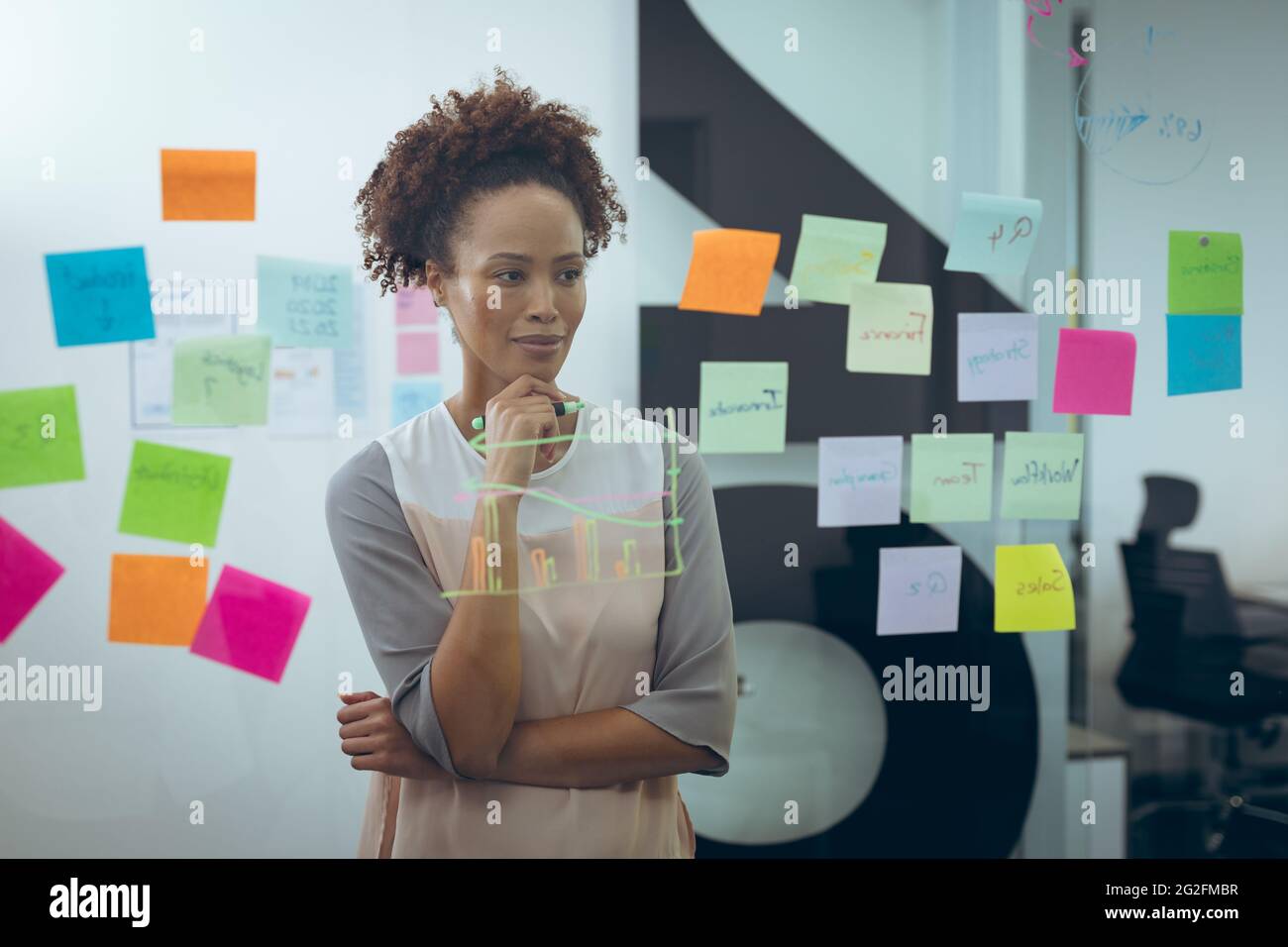 Mixed race businesswoman taking notes on glass board and thinking Stock ...