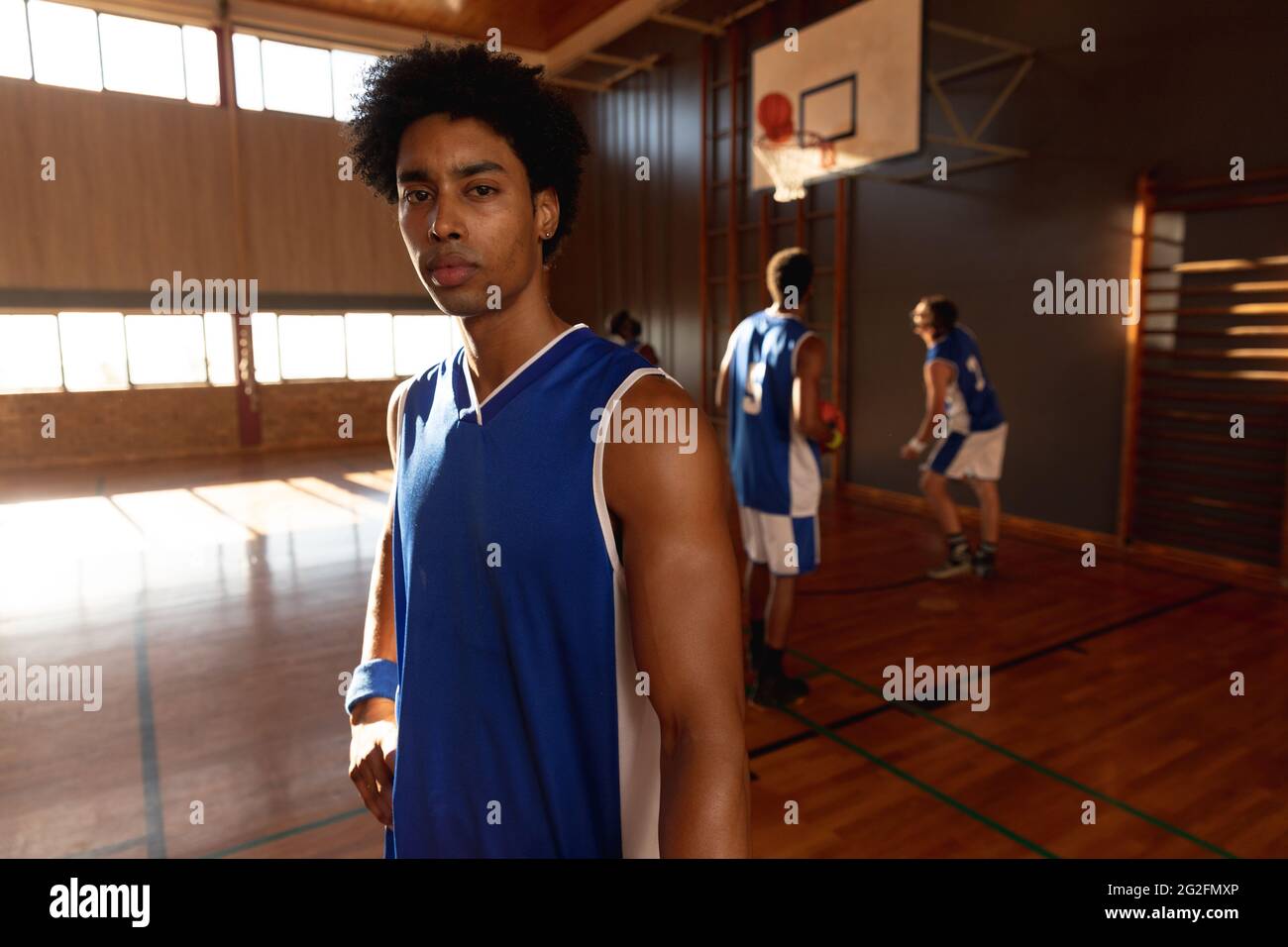 Portrait of mixed race male basketball player with team in background ...