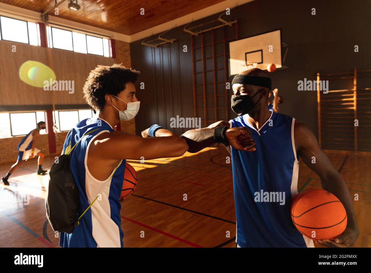 Diverse male basketball team greeting with elbows and wearing face ...