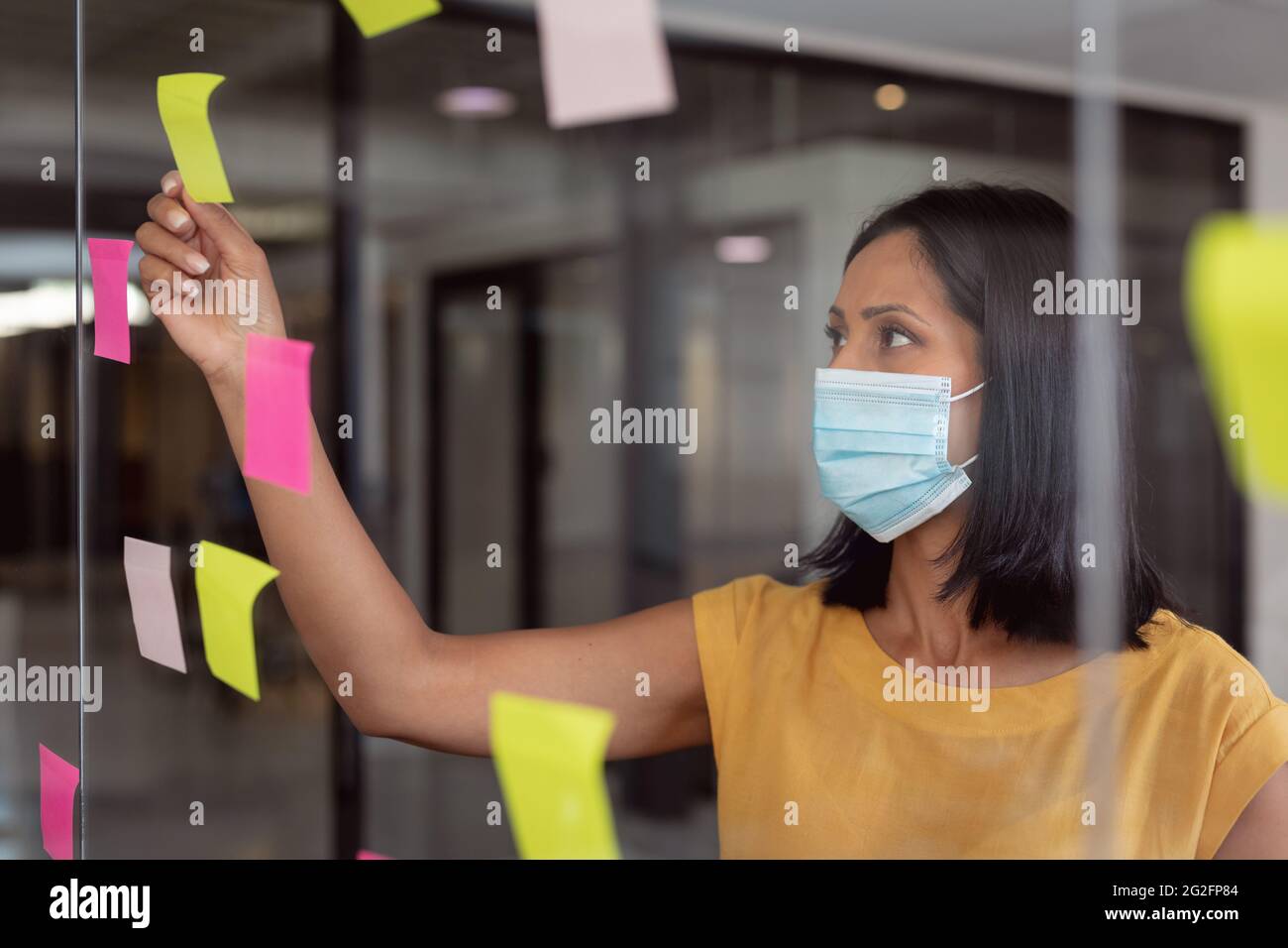 Caucasian businesswoman wearing face mask brainstorming, reading ...