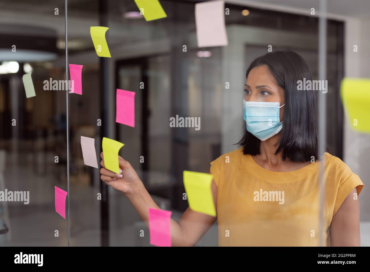 Caucasian businesswoman wearing face mask brainstorming, reading ...