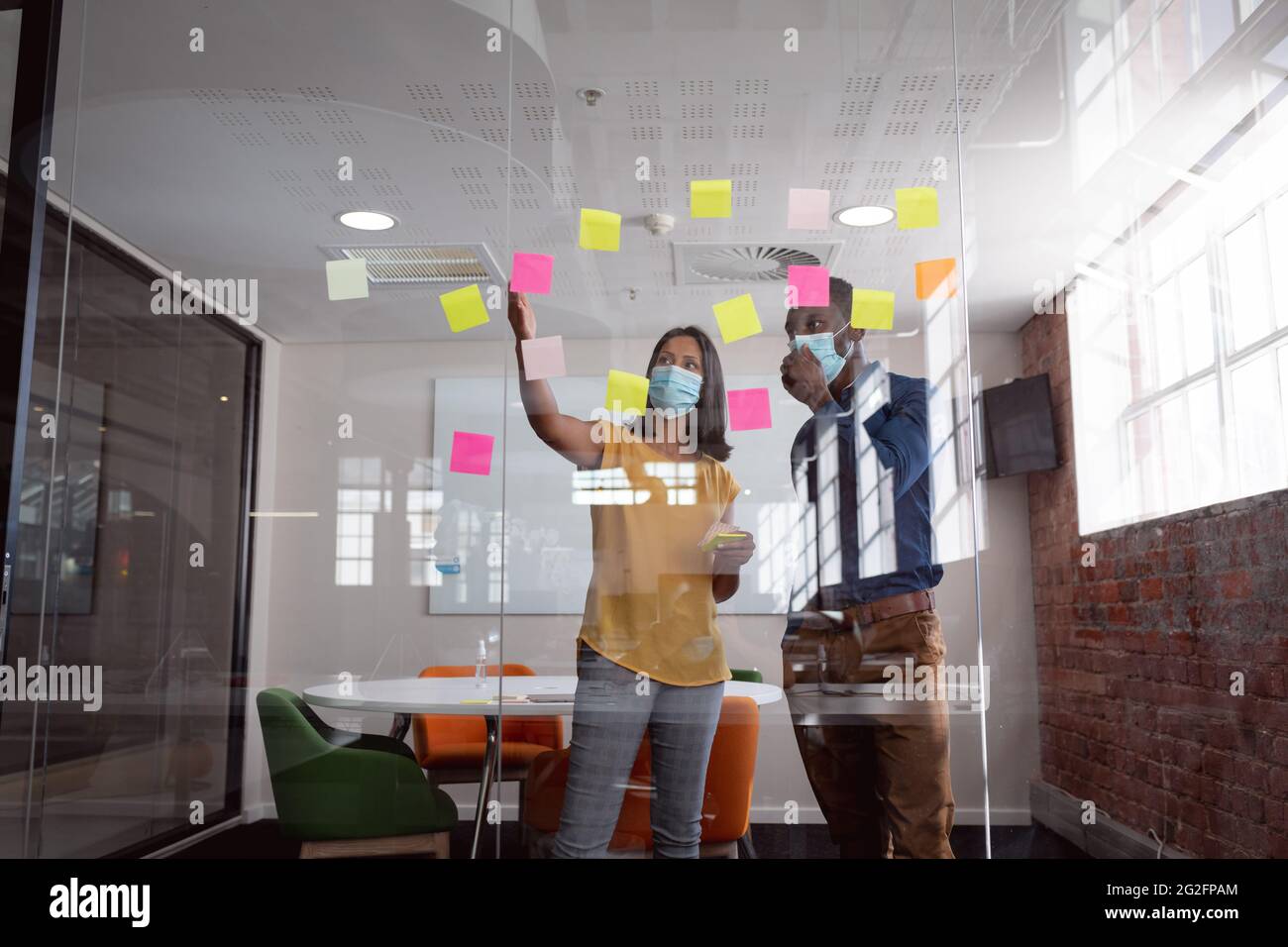 Diverse male and female colleague in face masks brainstorming, reading ...