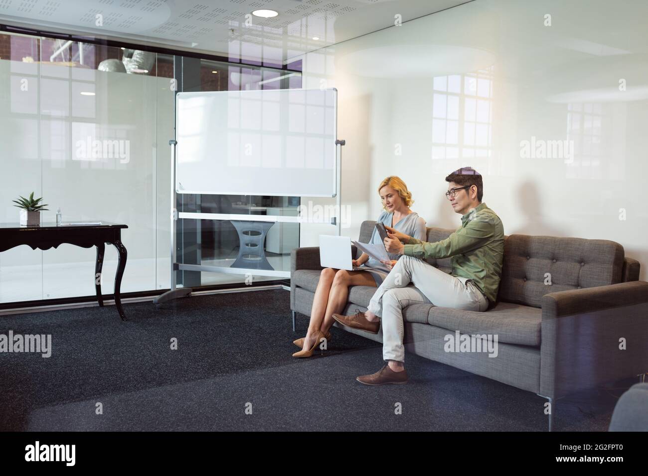 Diverse male and female colleague sitting in office lounge using tablet ...