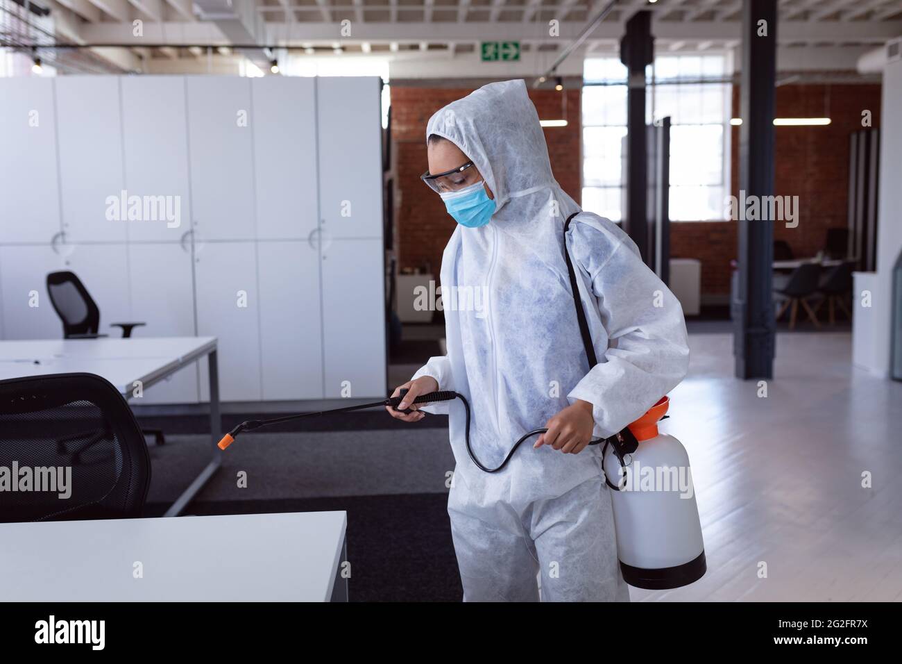 Cleaner wearing ppe suit, glasses and mask disinfecting office ...