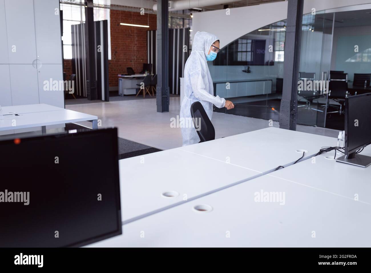 Cleaner wearing ppe suit, glasses and mask disinfecting office ...