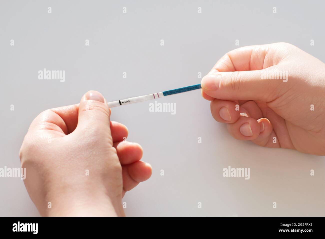 A woman holds a positive pregnancy test with two stripes on a light ...