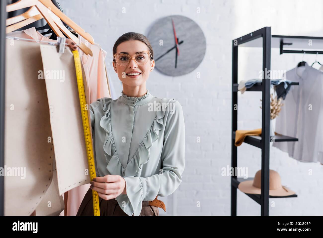 Seamstress smiling at camera while measuring sewing pattern in studio ...