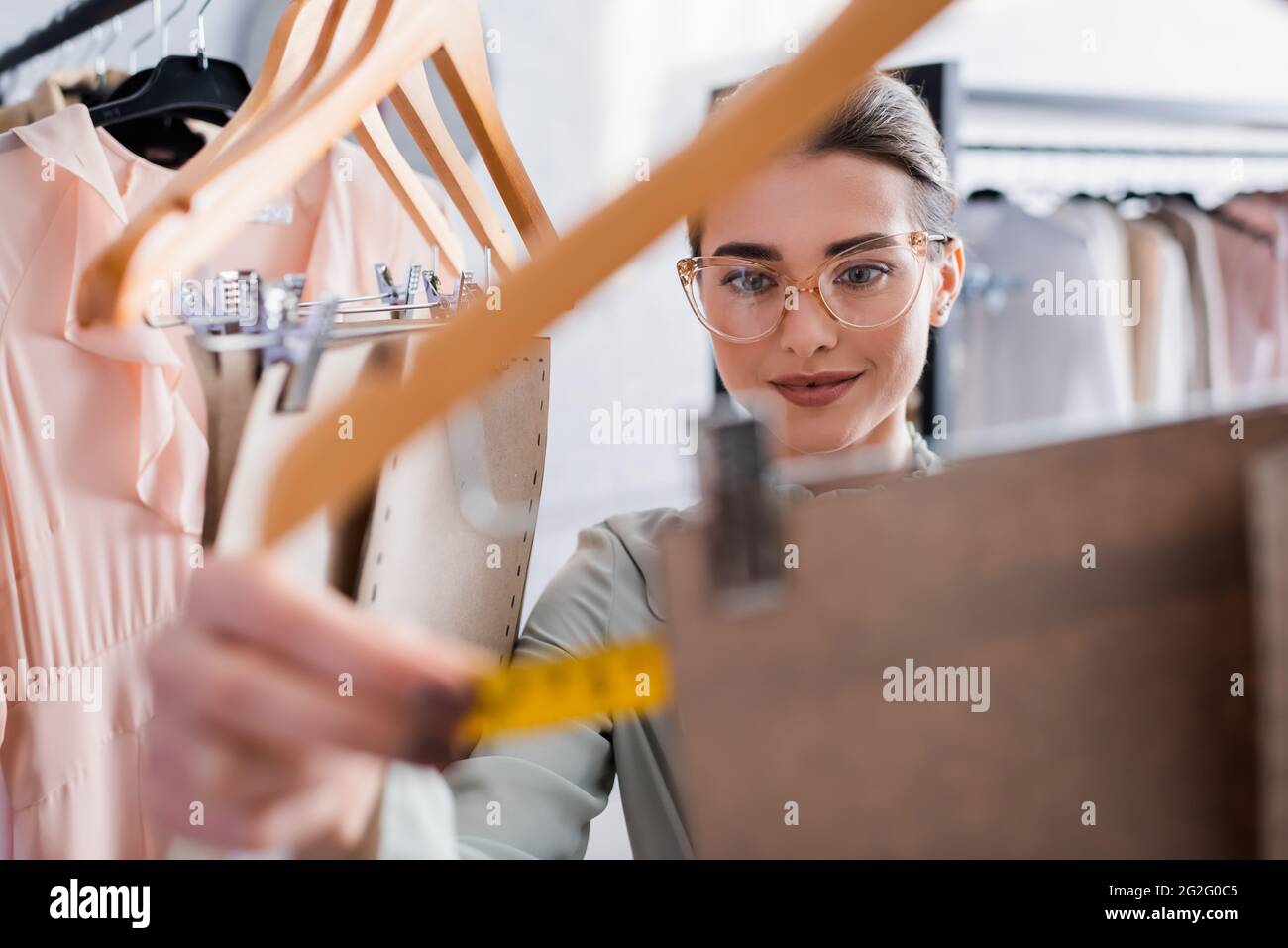 Cheerful designer measuring sewing pattern on blurred foreground Stock ...