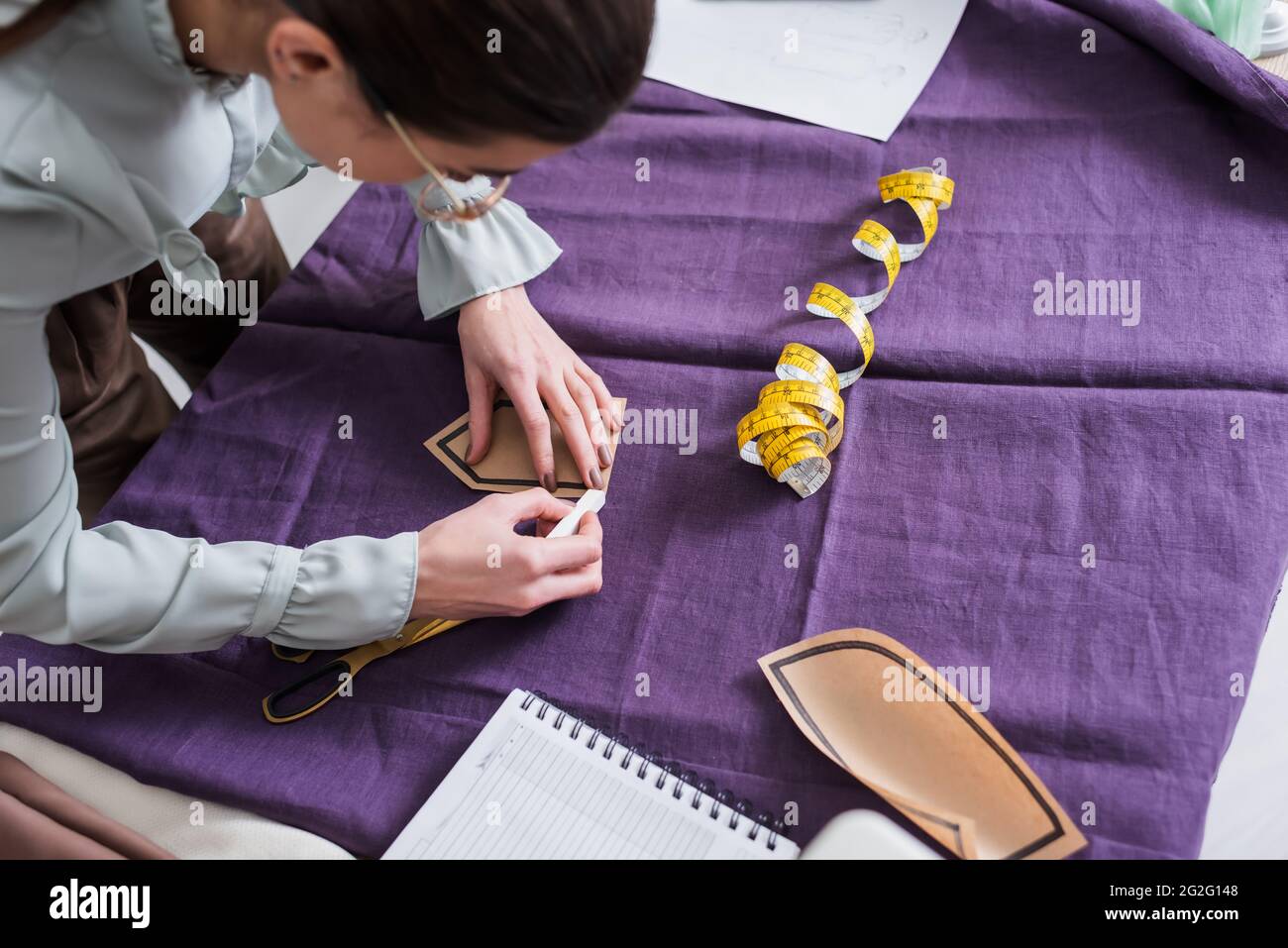 Overhead view of seamstress marking cloth and holding sewing pattern ...