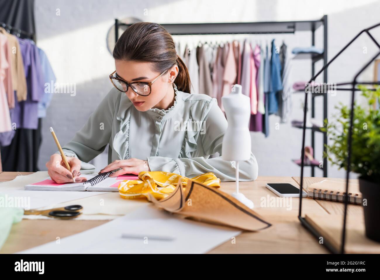 Designer writing on notebook near smartphone and cloth in studio Stock ...