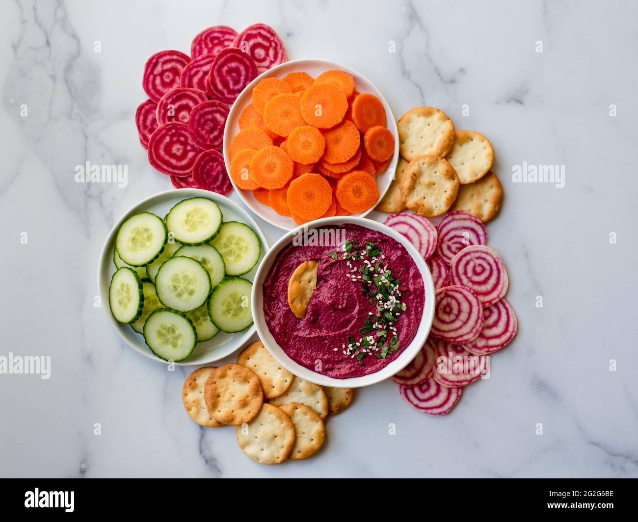 Bowl of beet hummus, vegetables and crackers on white marble counter ...
