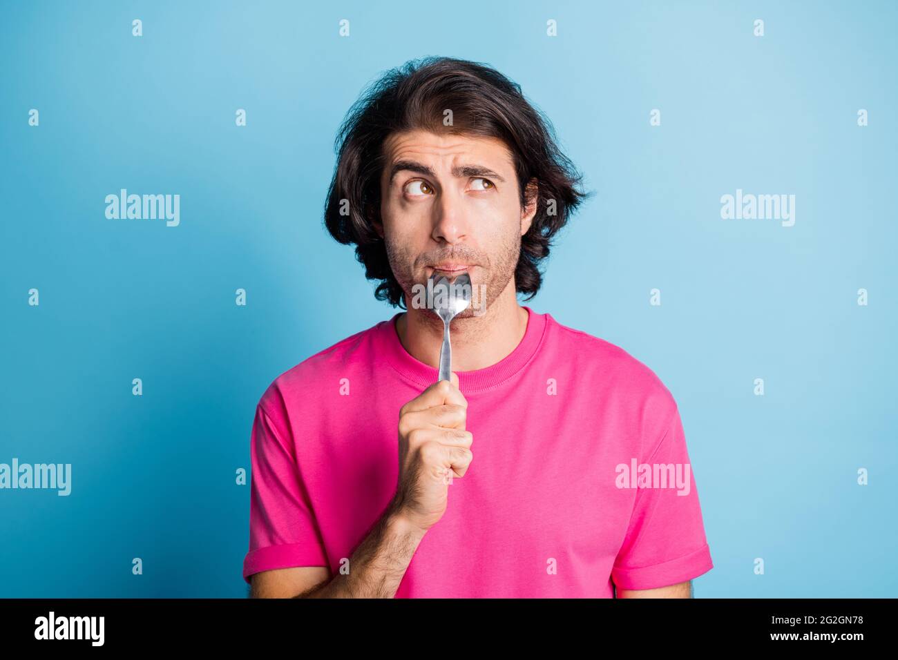 Portrait of attractive bewildered guy licking spoon counting calories ...