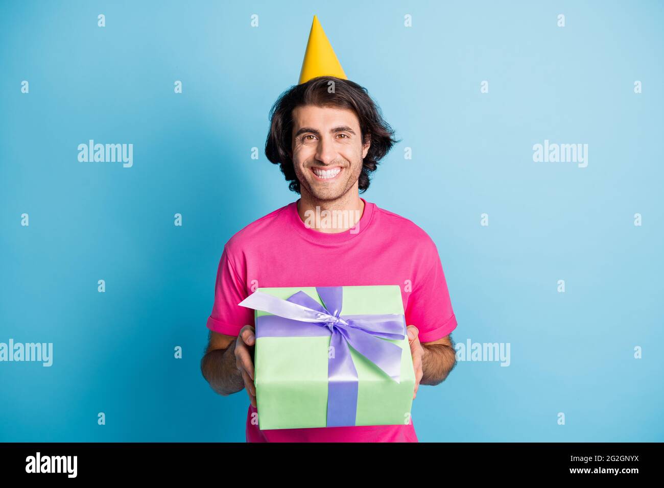 Portrait of attractive cheerful guy wear festal cap holding in hands ...