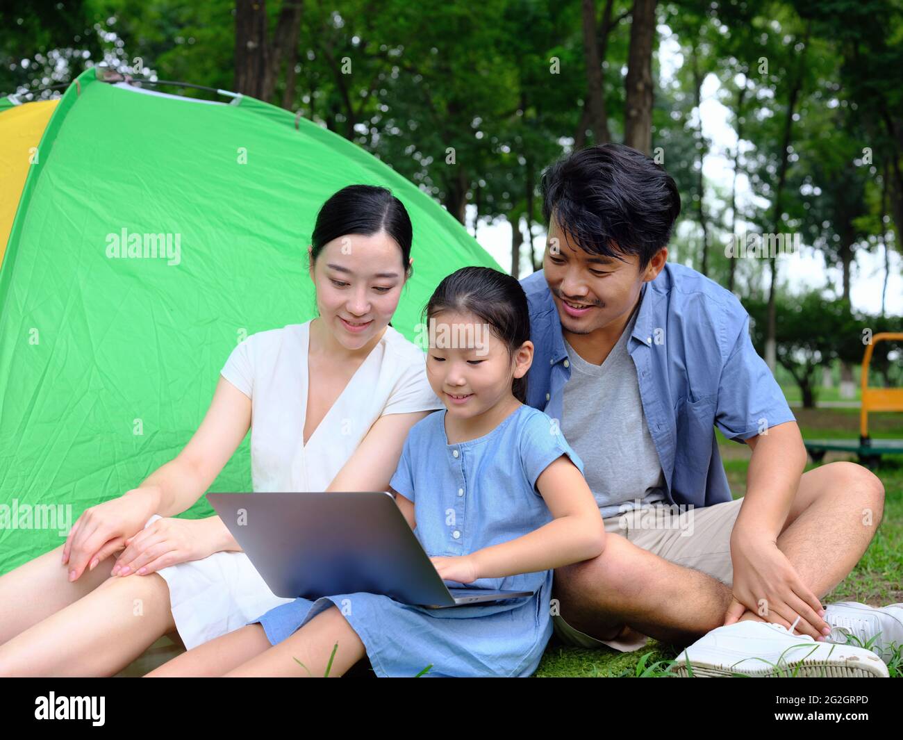 Happy family of three use computer to surf the Internet outdoors high ...