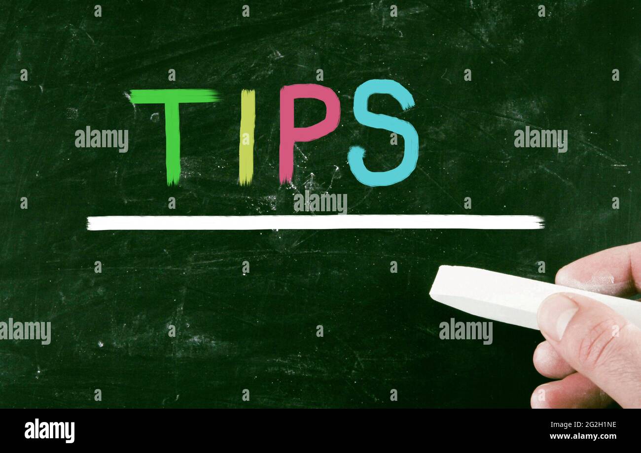 Male hand holding a piece of chalk and "TIPS" note on the blackboard ...