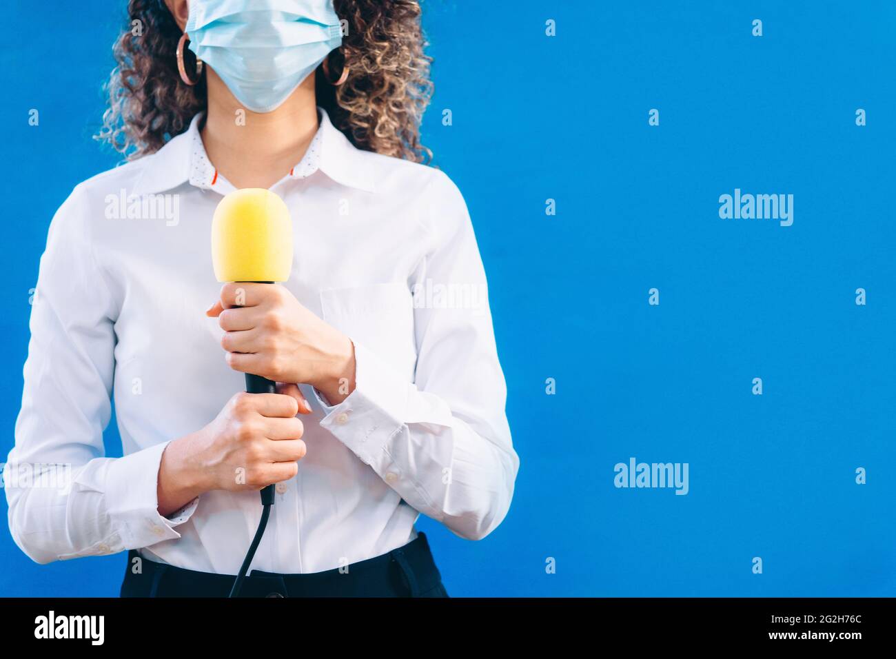 Female reporter wearing a medical face mask holding a yellow microphone ...