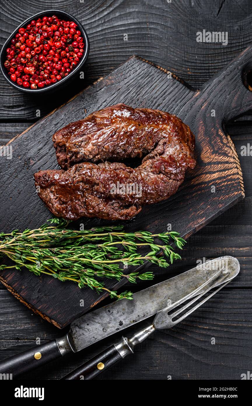 BBQ grilled Hanging Tender steak on a wooden cutting board. Dark wooden ...