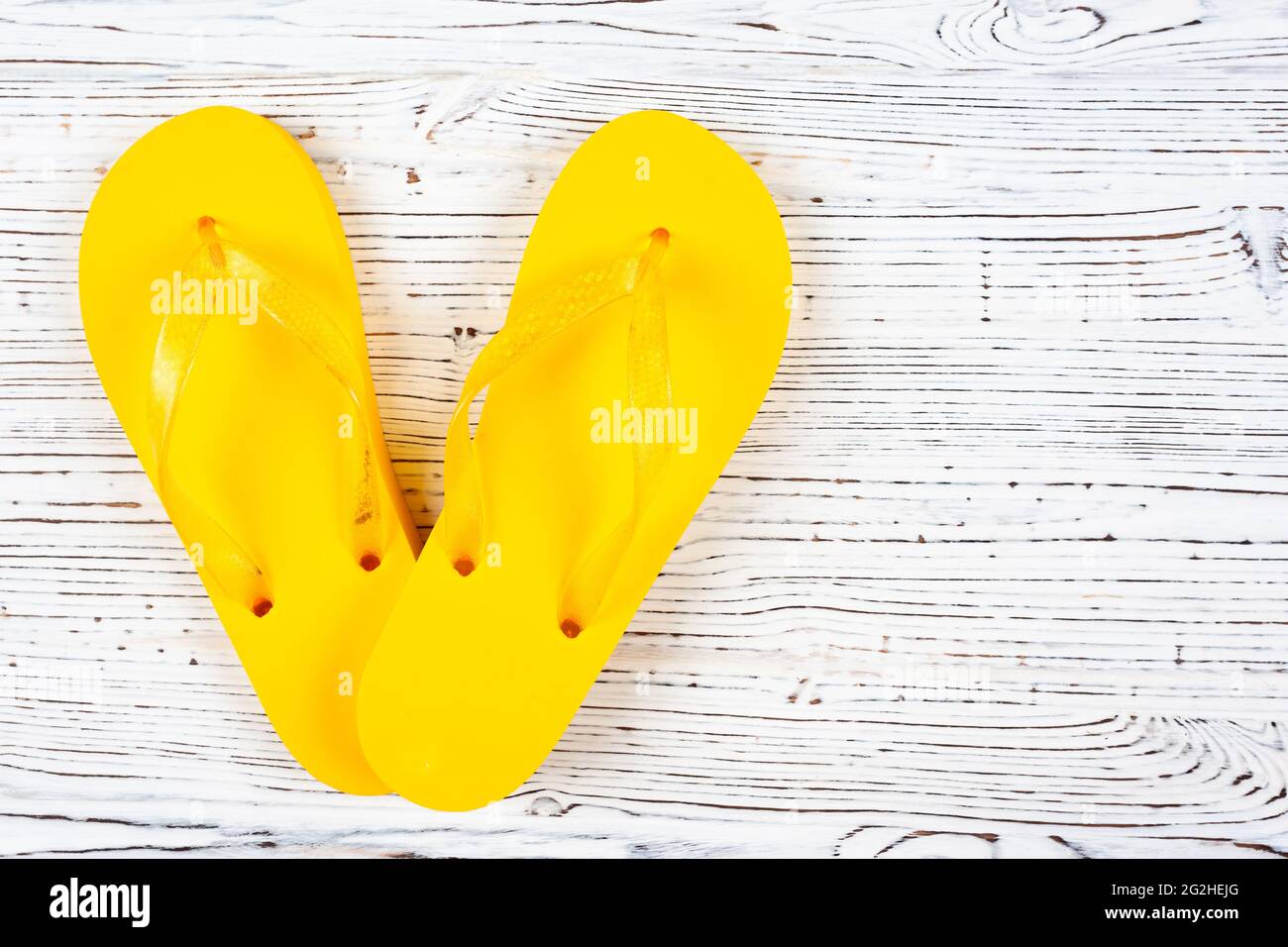 yellow rubber slippers on a white wooden background, view from above ...