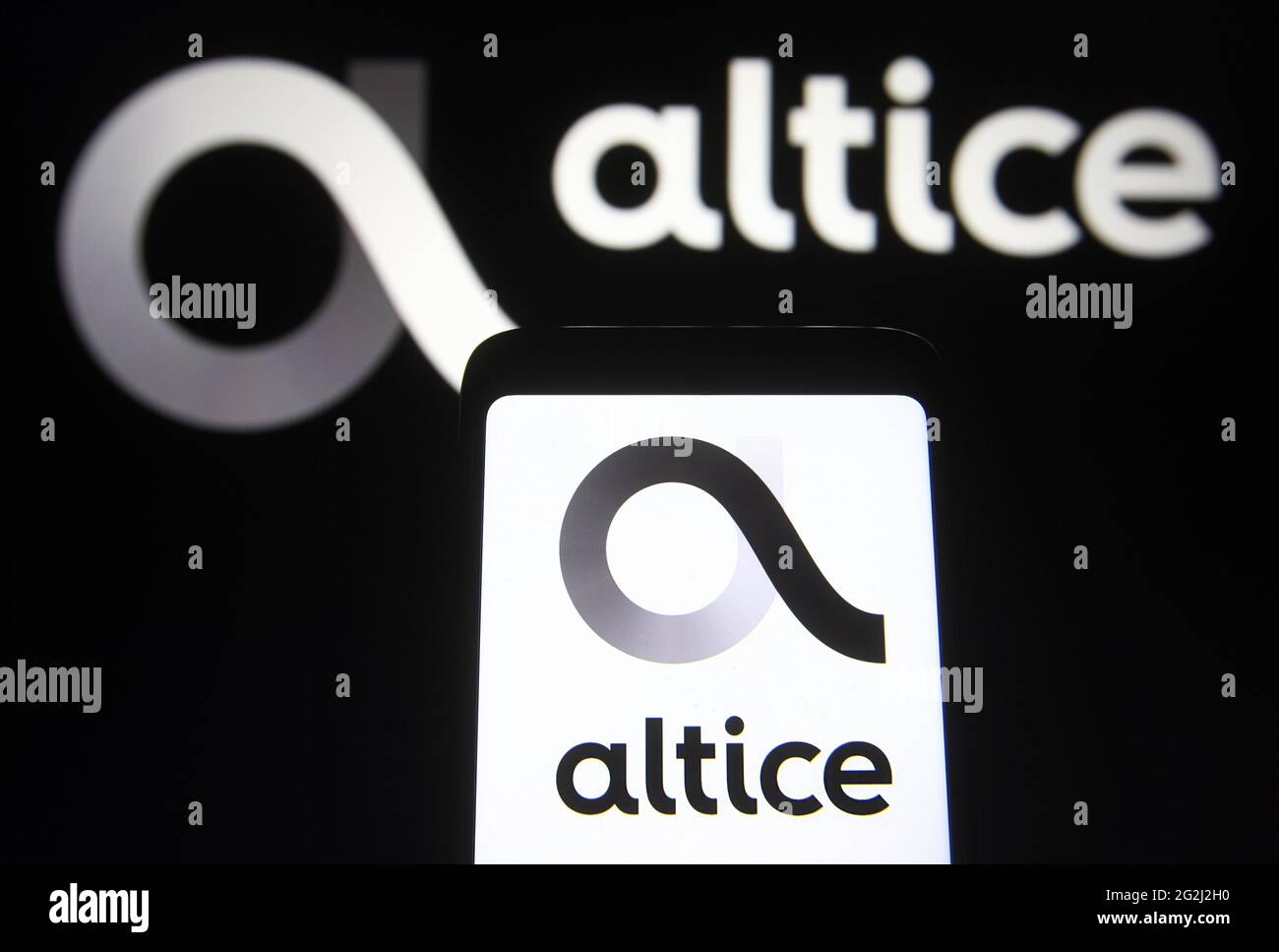 In this photo illustration an Altice USA logo logo is seen on a smartphone and a pc screen ...