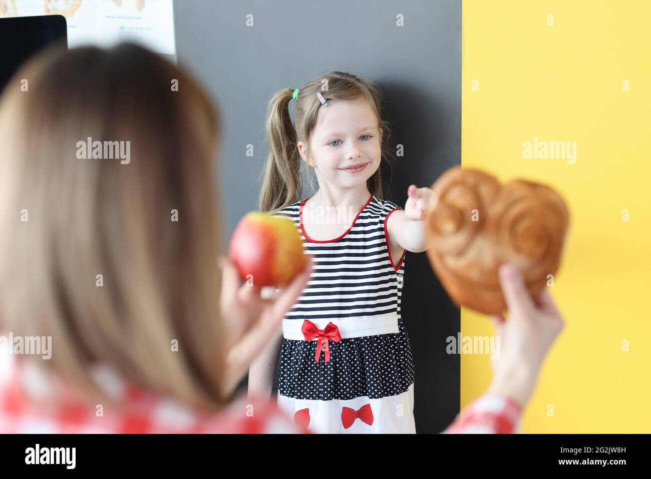 Mother offering bun or red apple to little girl Stock Photo - Alamy