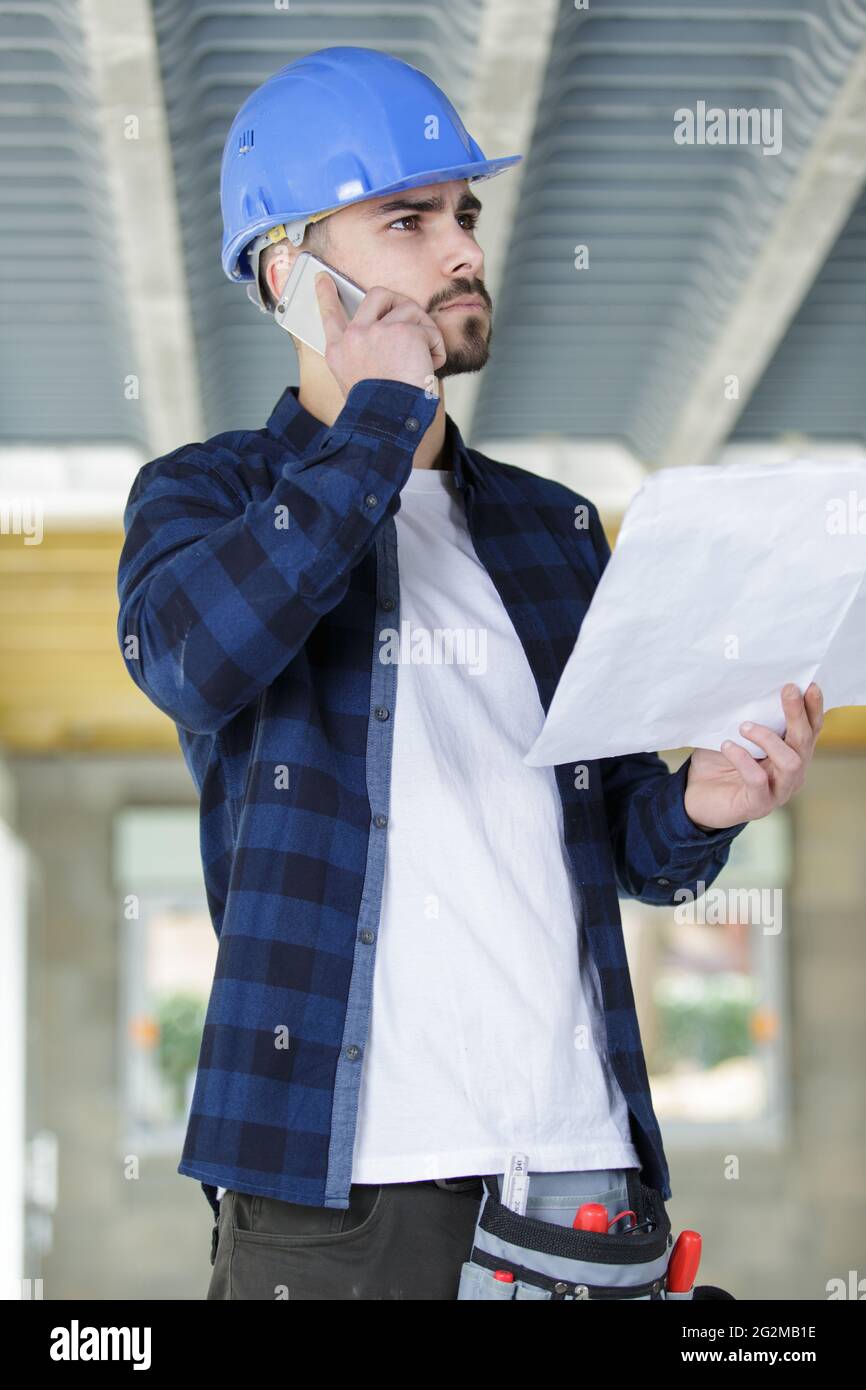 contractor on site holding plans and making telephone call Stock Photo ...