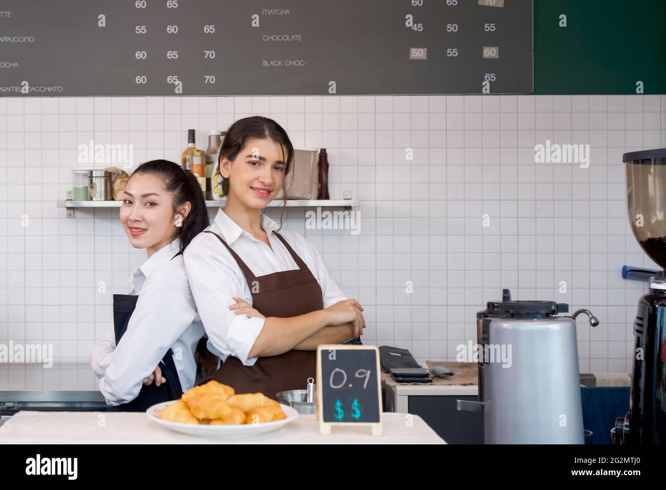 The shopkeeper and barista stand smiling with arms folded in front of a ...