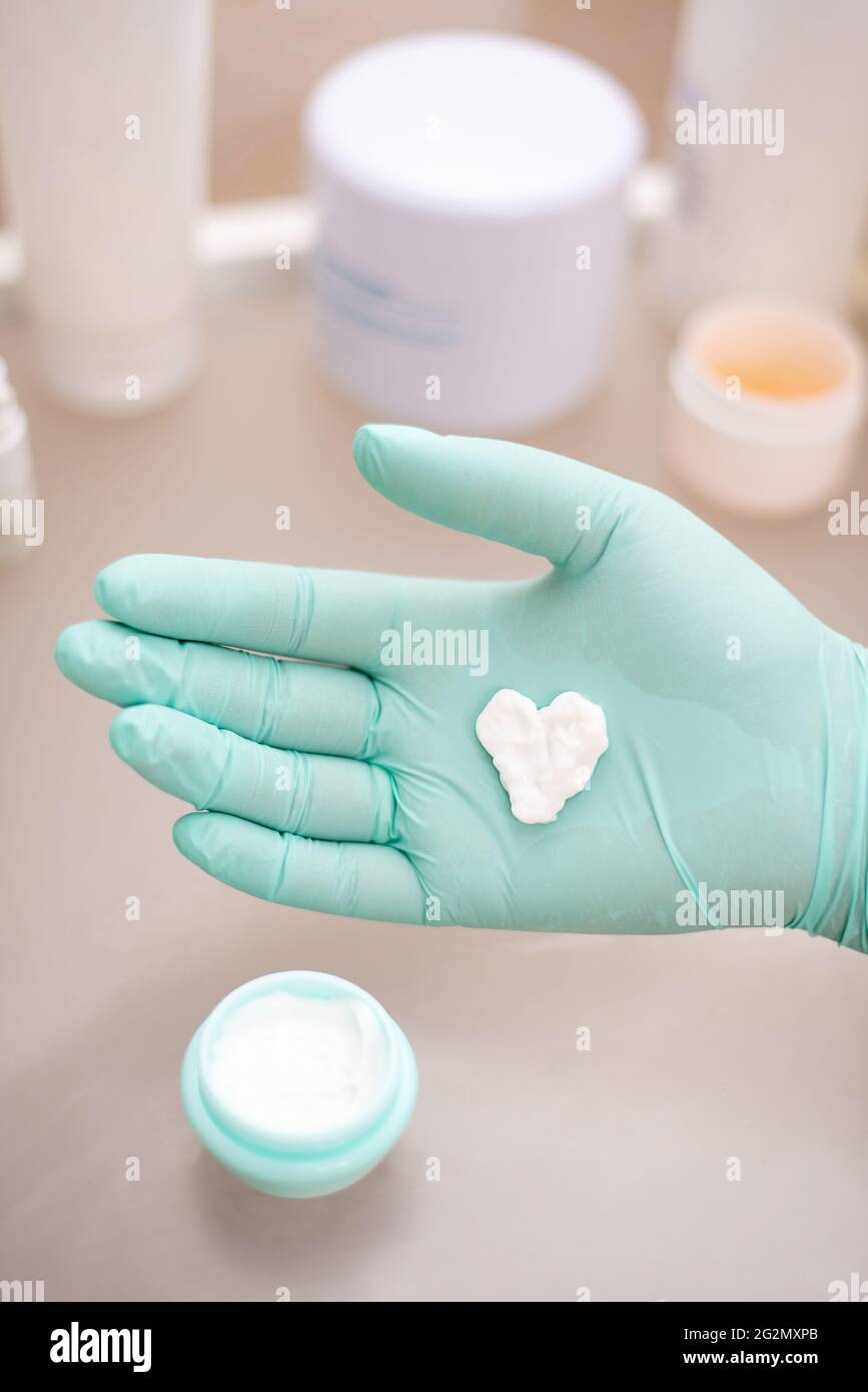 Heart shaped cream on the palm of a gloved hand and a jar with cream on ...