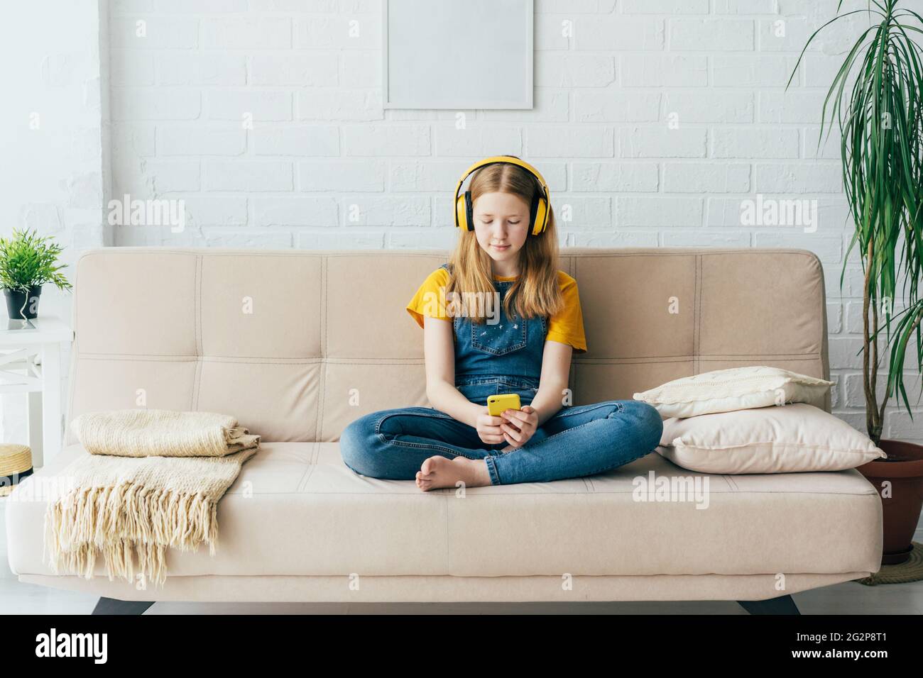 A teenage girl in wireless headphones with a mobile phone sits on the ...