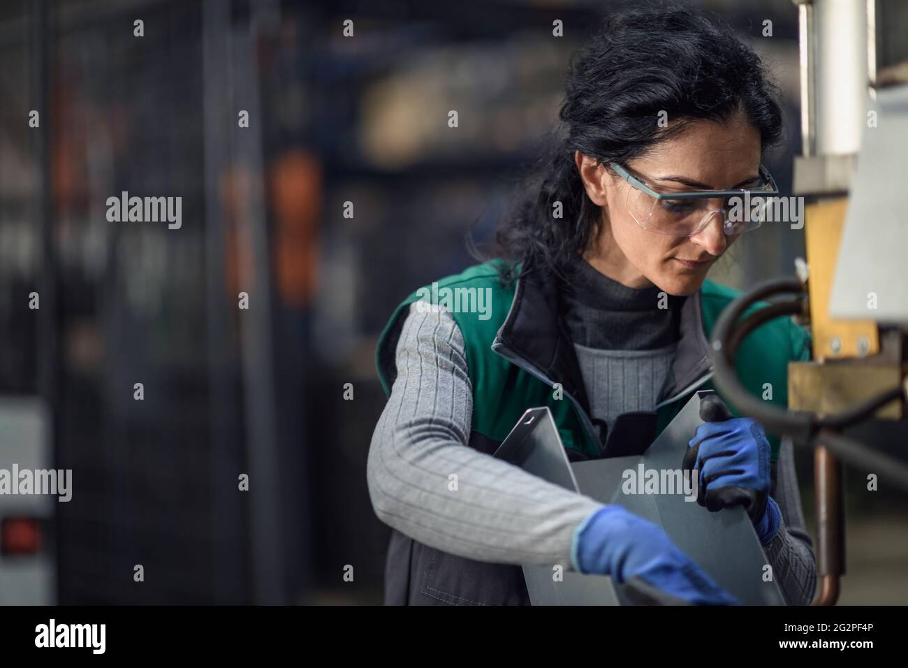 Woman worker wearing safety goggles control lathe machine to drill ...