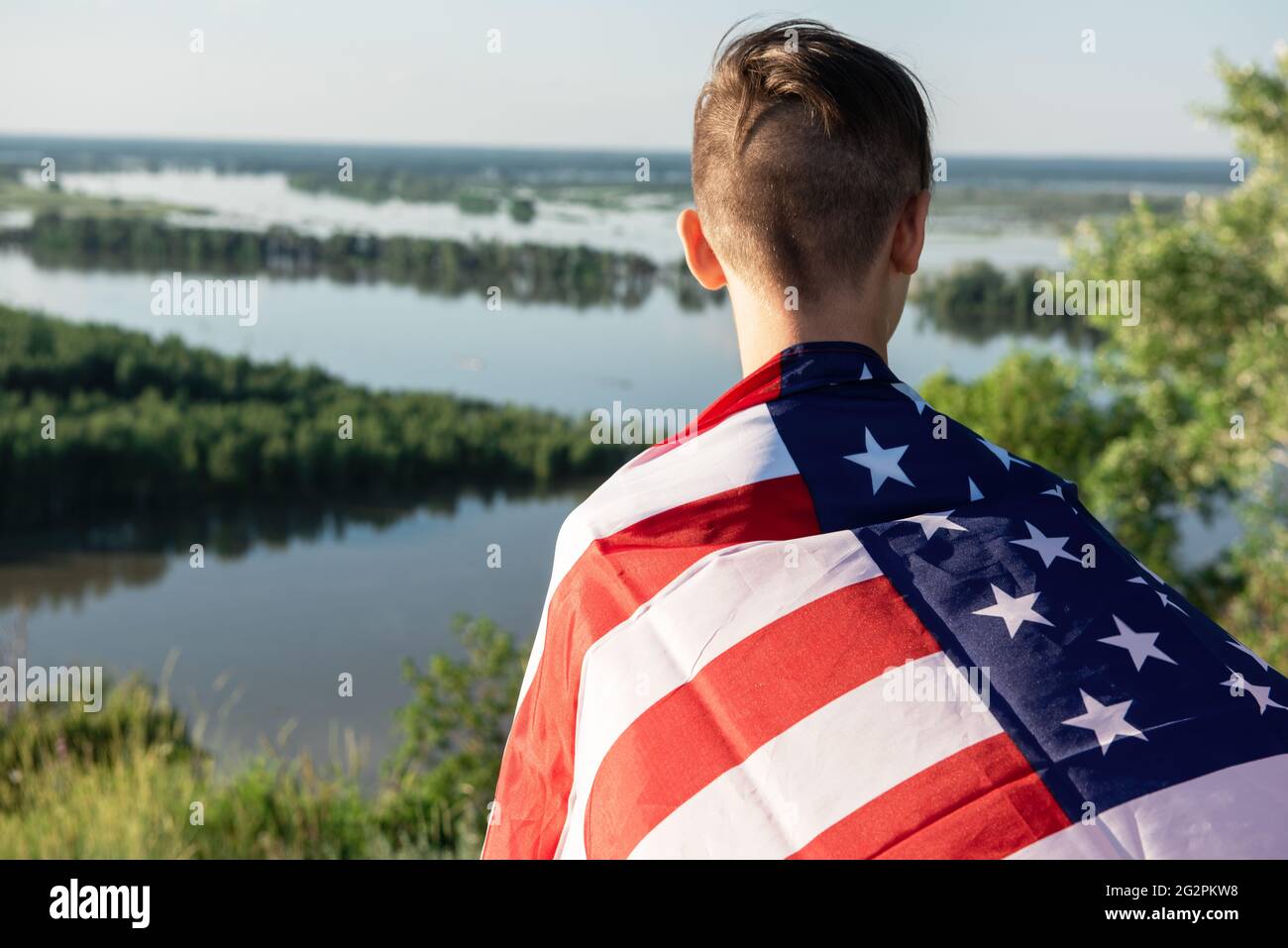 Blonde boy waving national USA flag outdoors over blue sky at the river ...
