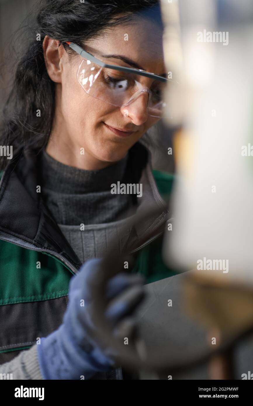 Woman worker wearing safety goggles control lathe machine to drill ...