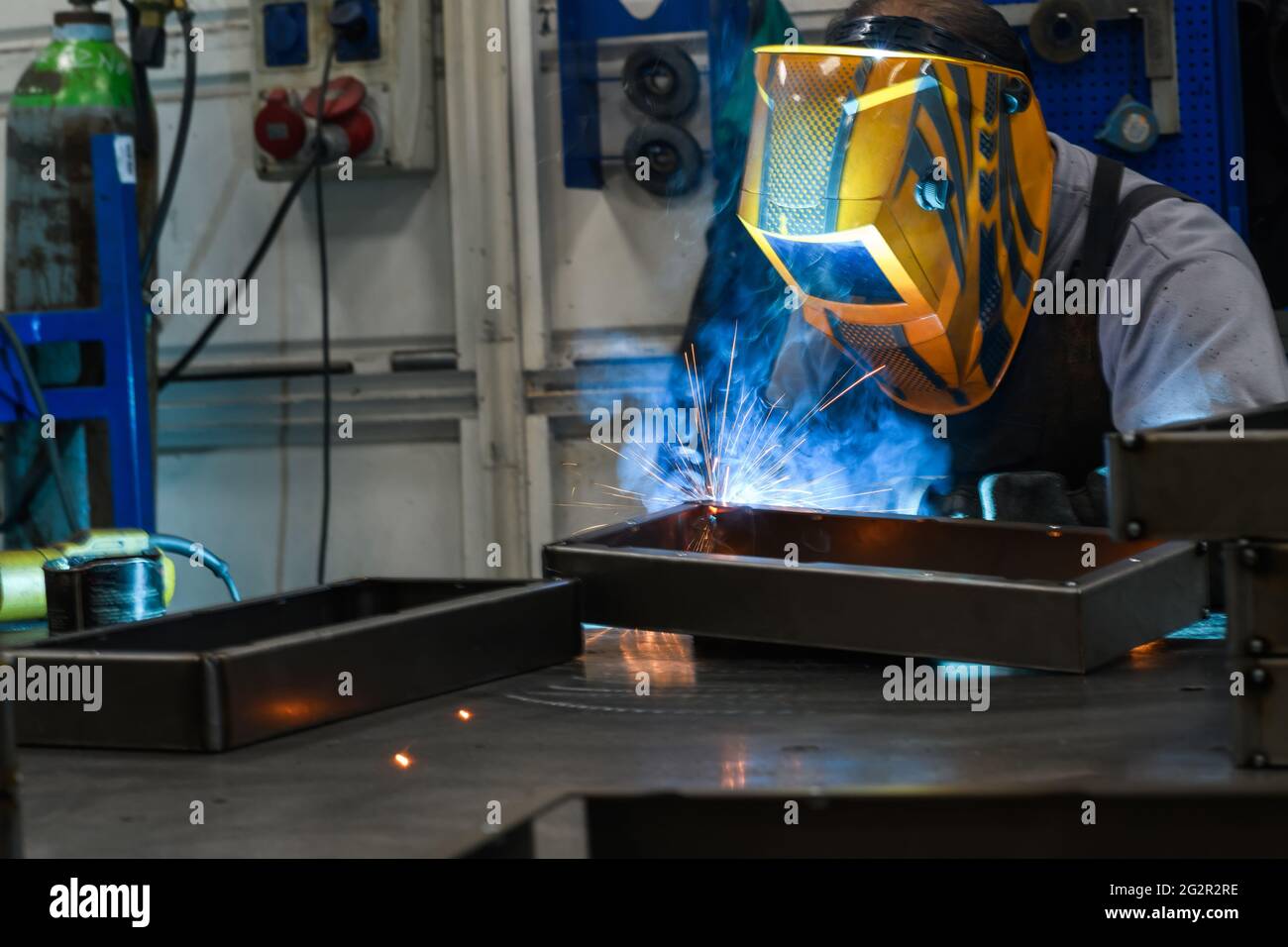 Professional welder performs work with metal parts in factory, sparks ...