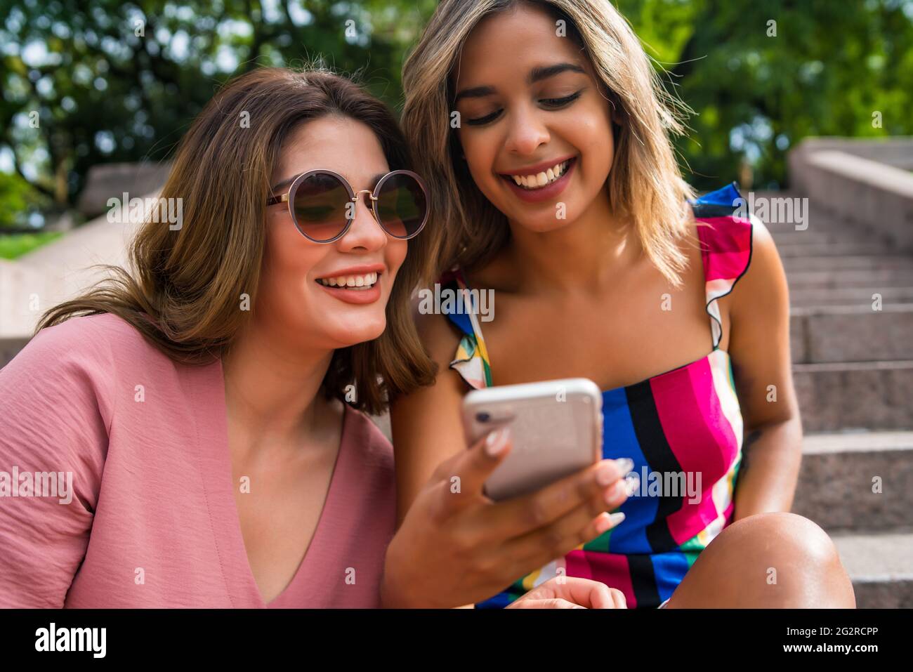 Two friends using mobile phone outdoors Stock Photo - Alamy