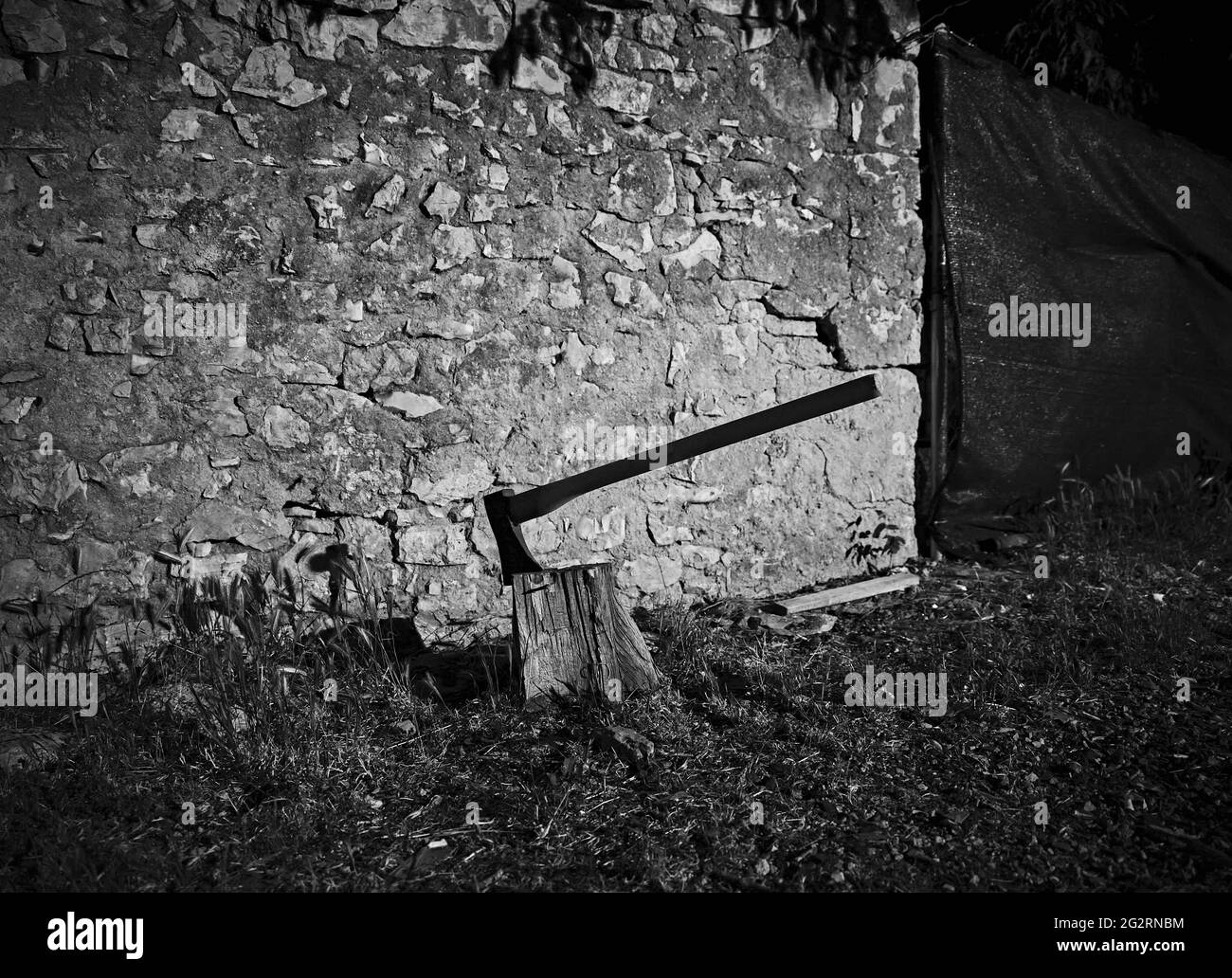 Grayscale shot of an ax stuck in a piece of wood on the background of a ...